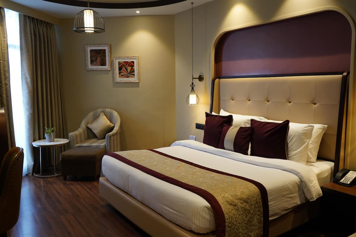 Quarto de hotel com uma cama grande, uma cadeira, uma mesinha com uma planta e obras de arte na parede.