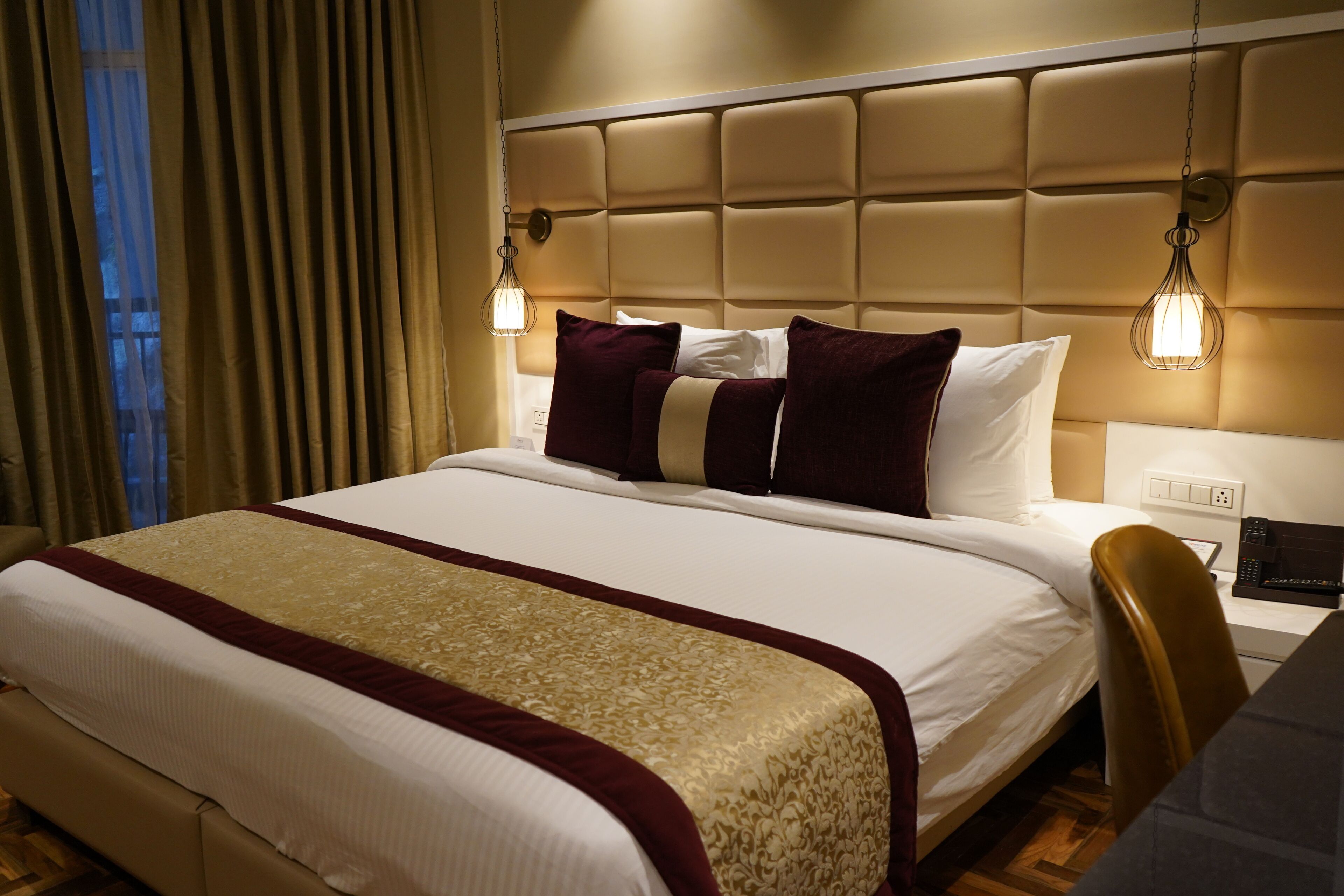 Quarto de hotel com cama grande, cabeceira com design acolchoado, duas luminárias de cabeceira e uma mesa com telefone.