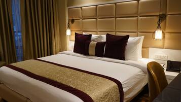 Quarto de hotel com cama grande, cabeceira com design acolchoado, duas luminárias de cabeceira e uma mesa com telefone.
