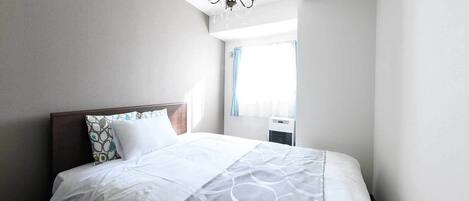 Quarto de hotel com cama, um candelabro, janela com cortinas e unidade de ar condicionado.
