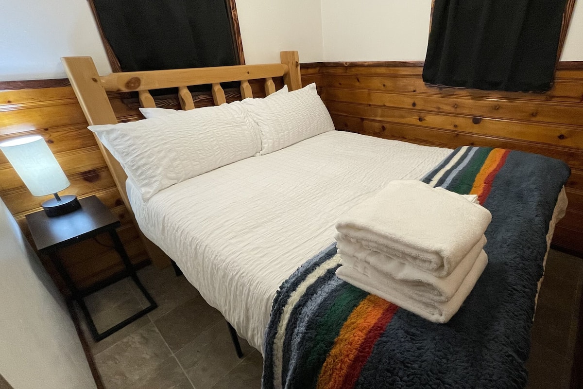 Uma cama de solteiro com cabeceira de madeira, mesa de cabeceira e um cobertor listrado e colorido.
