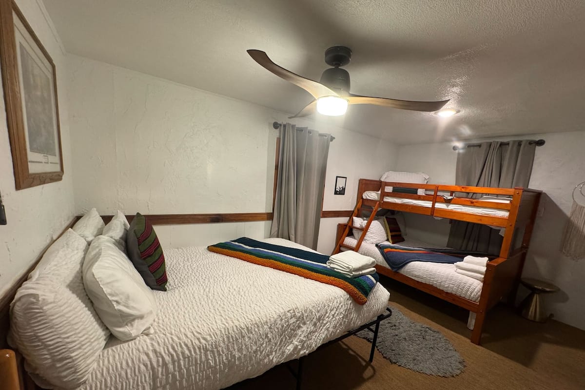 Quarto com uma cama de solteiro, uma cama beliche, um ventilador de teto e um tapete pequeno.