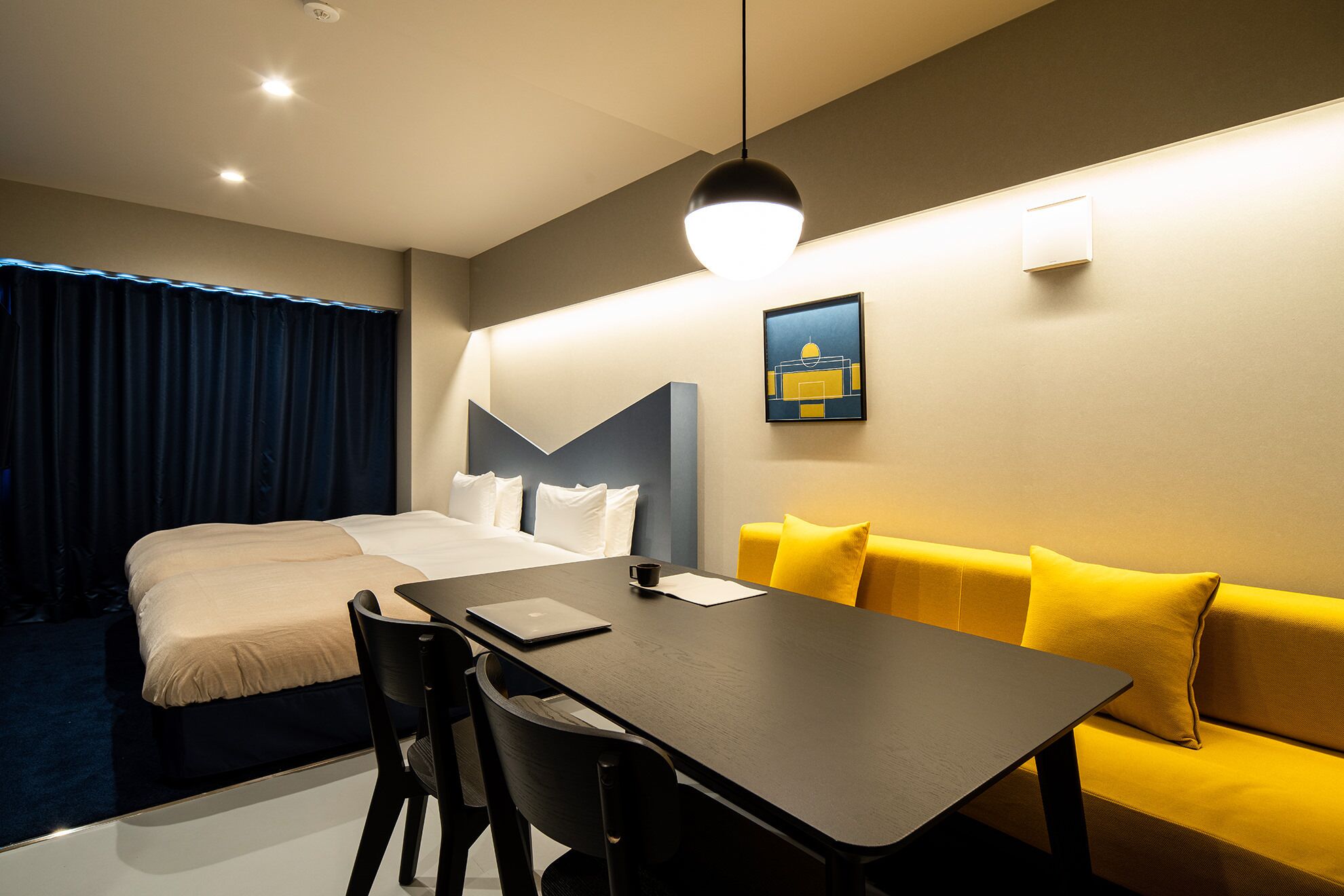 Quarto de hotel moderno com uma cama, uma escrivaninha e um sofá amarelo.