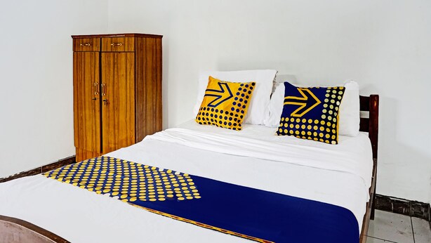 Uma cama com colcha estampada em azul e amarelo, duas almofadas com desenhos em azul e amarelo, e um guarda-roupa de madeira.