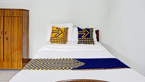 Uma cama com colcha estampada, duas almofadas com desenhos geométricos e um guarda-roupa de madeira.