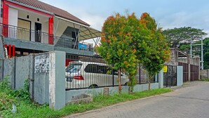 Um edifício com fachada vermelha e branca, uma varanda coberta e uma árvore com flores laranjas.