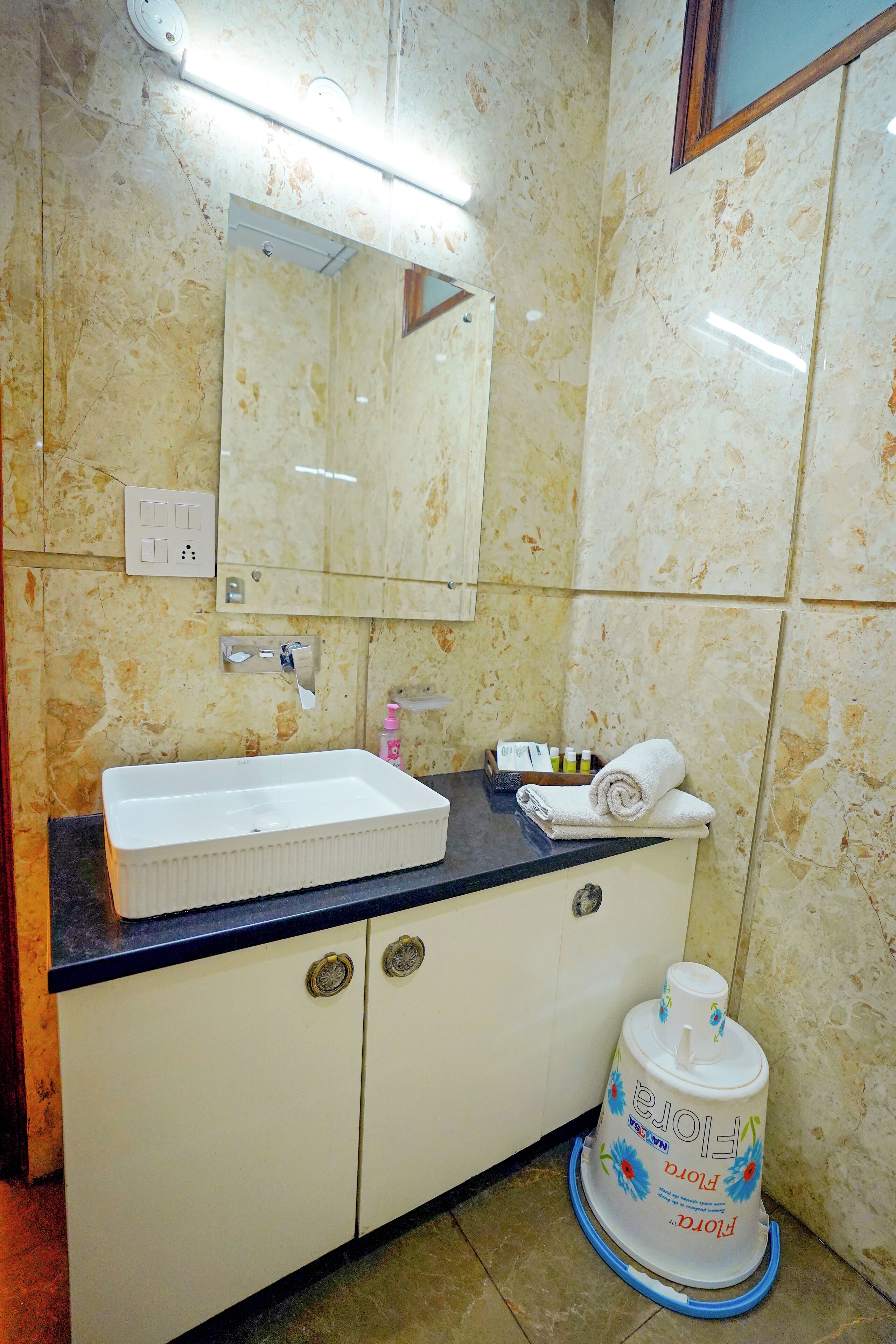 Casa de banho com lavatório branco, espelho e armários. Há uma toalha e artigos de higiene no balcão.