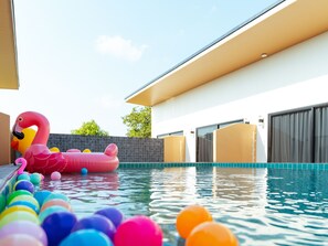 Piscina com flamingos infláveis e bolas coloridas, rodeada por um edifício moderno com grandes janelas e um espaço de varanda coberto.