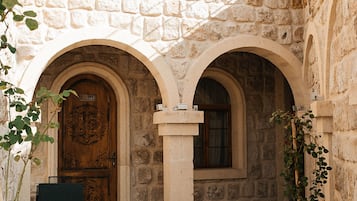 Um pátio de pedra com arcadas, uma porta de madeira e uma mesa com cadeiras.