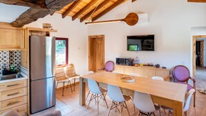 Cozinha moderna com vigas de madeira, geladeira de aço inoxidável e área de jantar com mesa e cadeiras de madeira.