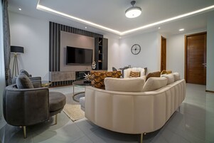 Uma sala de estar moderna com um sofá curvo, uma mesinha redonda e uma televisão de tela plana fixada na parede.