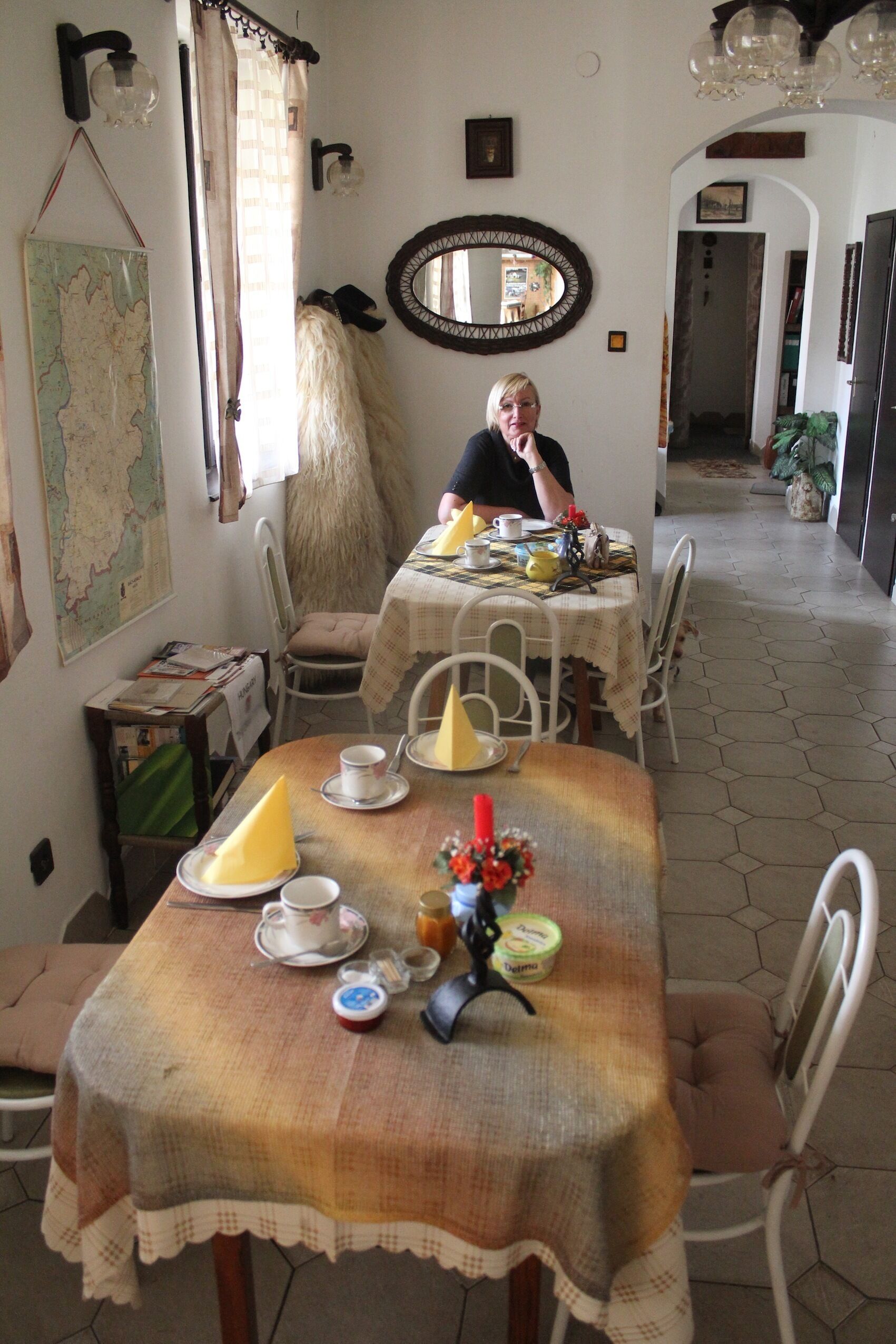 Uma área de refeições com uma mesa posta para dois, um mapa na parede e um espelho sobre a mesa.