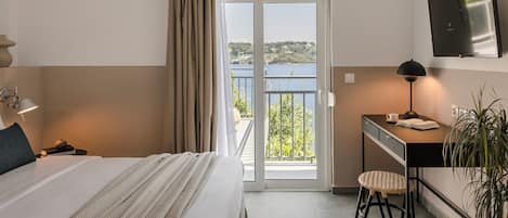 Quarto de hotel com cama, secretária com cadeira, televisão e varanda com vista para o mar.