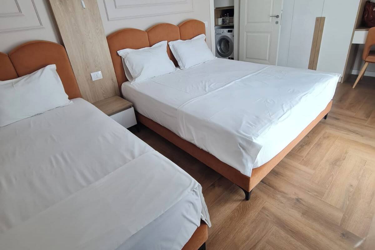 Quarto de hotel com duas camas, piso de madeira e uma máquina de lavar roupa ao fundo.