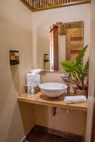 Casa de banho com toucador de madeira, lavatório branco, espelho e planta em vaso.