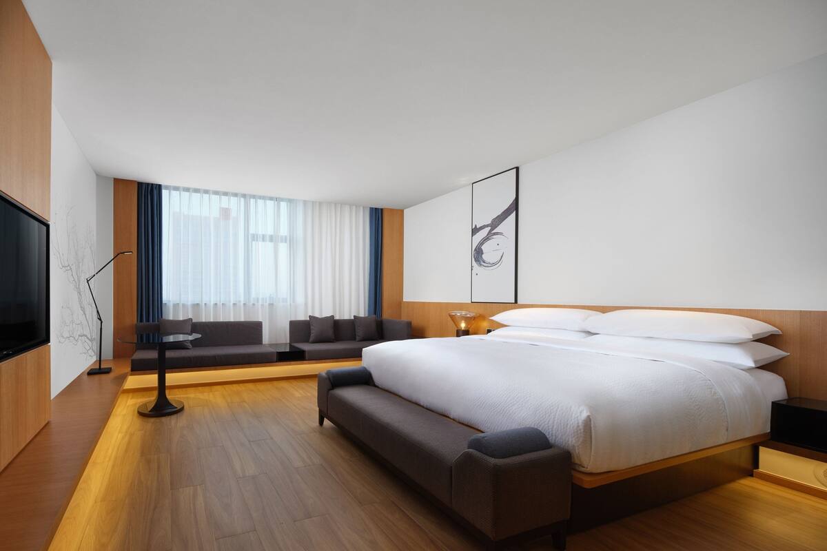 Quarto de hotel moderno com uma cama grande, um sofá, uma TV e uma mesa de trabalho.