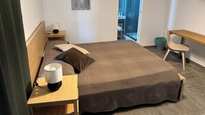 Um quarto com cama, mesa de cabeceira, abajur, cadeira e um quadro na parede.
