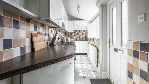 Cozinha com bancada de madeira escura, armários brancos e painel de azulejos.