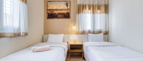 Quarto de hotel com duas camas de solteiro, uma mesa de cabeceira com abajur, um quadro na parede e uma janela com cortinas.