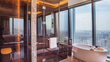 Quarto de hotel alto com vista para a cidade, uma banheira grande e uma área de estar com divisória de vidro.
