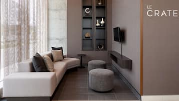 Uma sala de estar moderna com um sofá, pufes, uma televisão e uma estante com objetos decorativos.