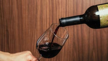Uma mão segurando uma taça de vinho recebendo vinho tinto de uma garrafa.