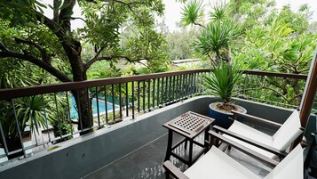 Uma varanda com um vaso de planta, uma mesa pequena e uma piscina ao fundo.