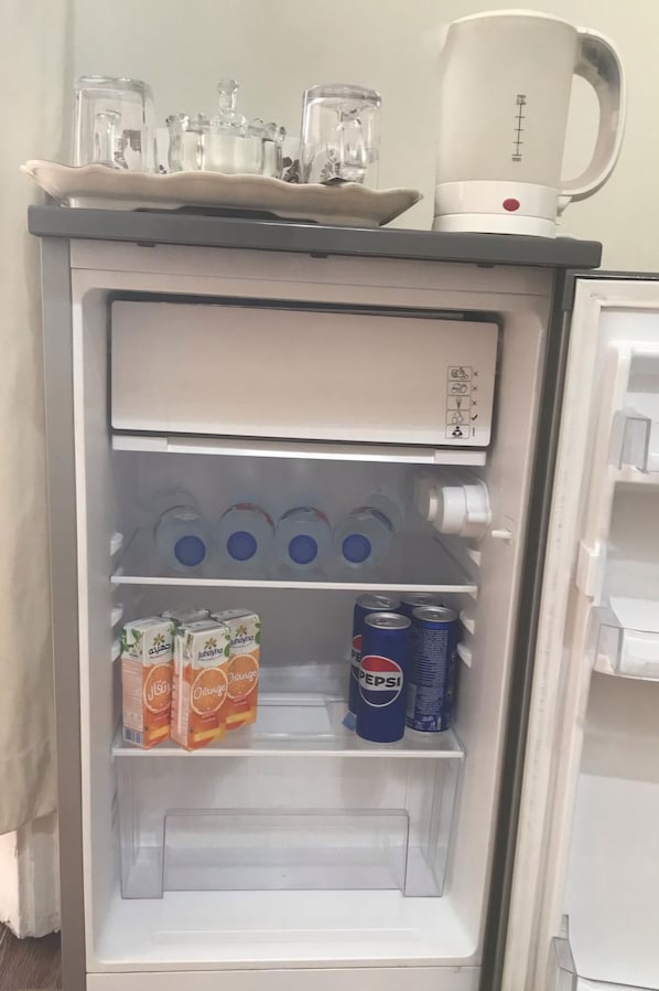 Geladeira com prateleiras contendo garrafas de água, caixas de suco e latas de bebidas.