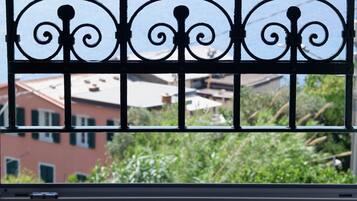 Uma janela com grade metálica decorativa, vista de edifícios, e uma mesa com chaleira e chávenas.