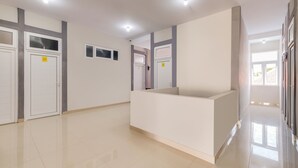 Corredor amplo e bem iluminado com balcão de recepção, várias portas e piso ladrilhado.