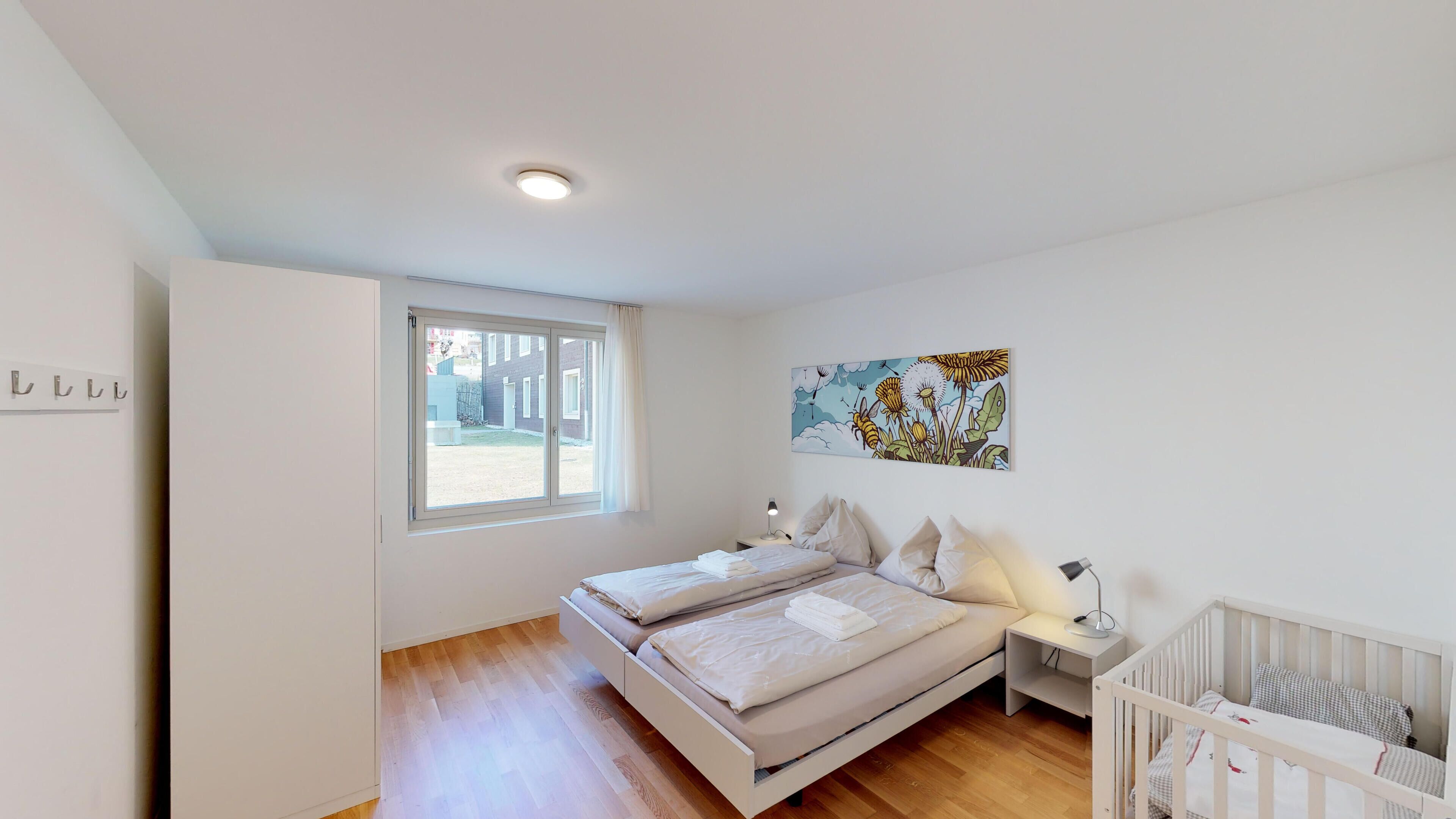 Quarto com cama, mesas de cabeceira, berço, janela e luminária no teto.
