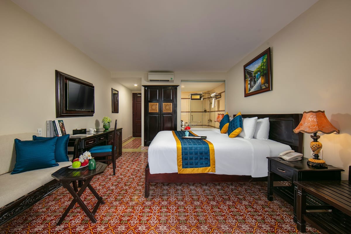 Quarto de hotel com cama, sofá, escrivaninha, cadeira, mesa e zona de chuveiro.
