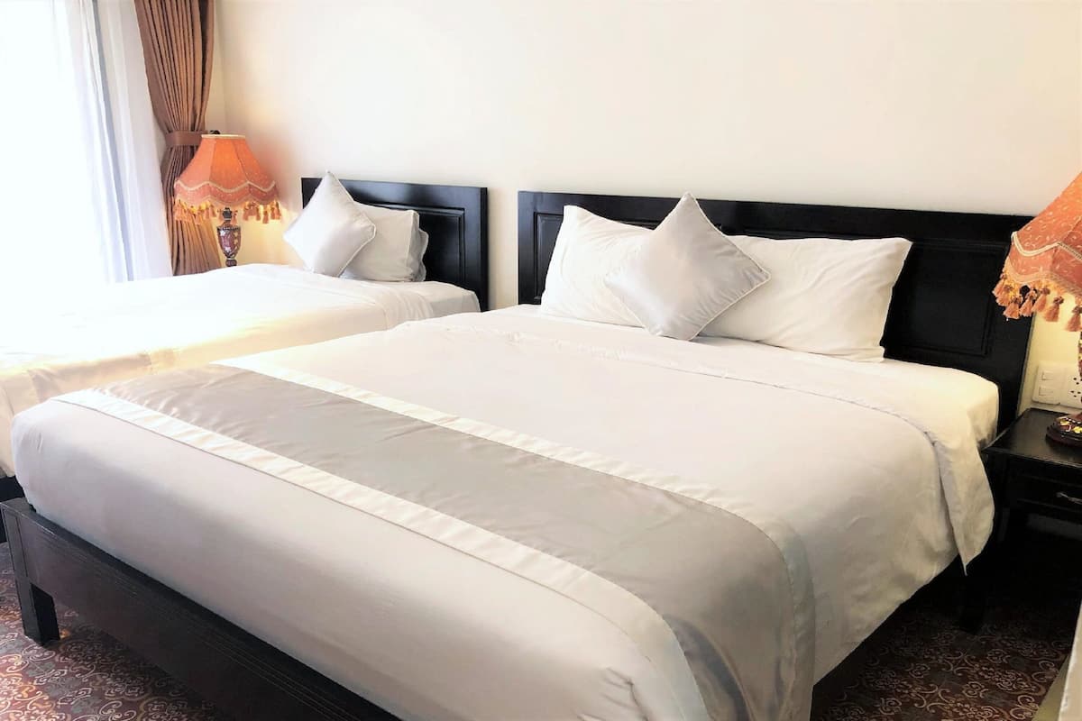 Quarto de hotel com duas camas, mesa de cabeceira, abajur e carpete estampado.