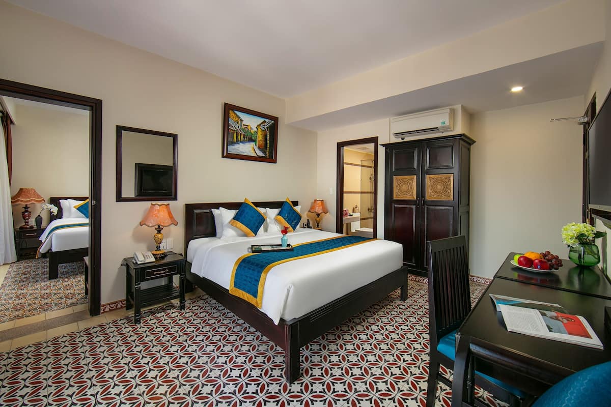 Quarto de hotel com uma cama grande, uma escrivaninha com cadeira, um espelho e um quadro na parede.