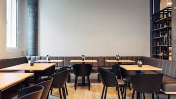 Um restaurante moderno com cabines e mesas, um pilar grande e uma estante com plantas.