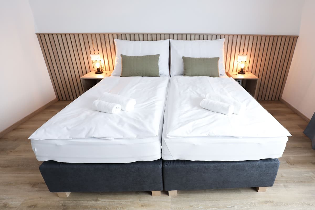 Uma cama de casal com lençóis brancos, duas almofadas e duas mesas de cabeceira com abajures.