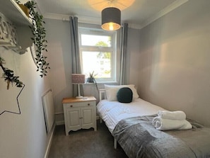 Um quarto com uma cama, mesa de cabeceira, abajur e janela com cortinas.
