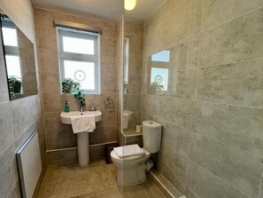 Casa de banho compacta com lavatório pedestal, sanita e janela pequena.