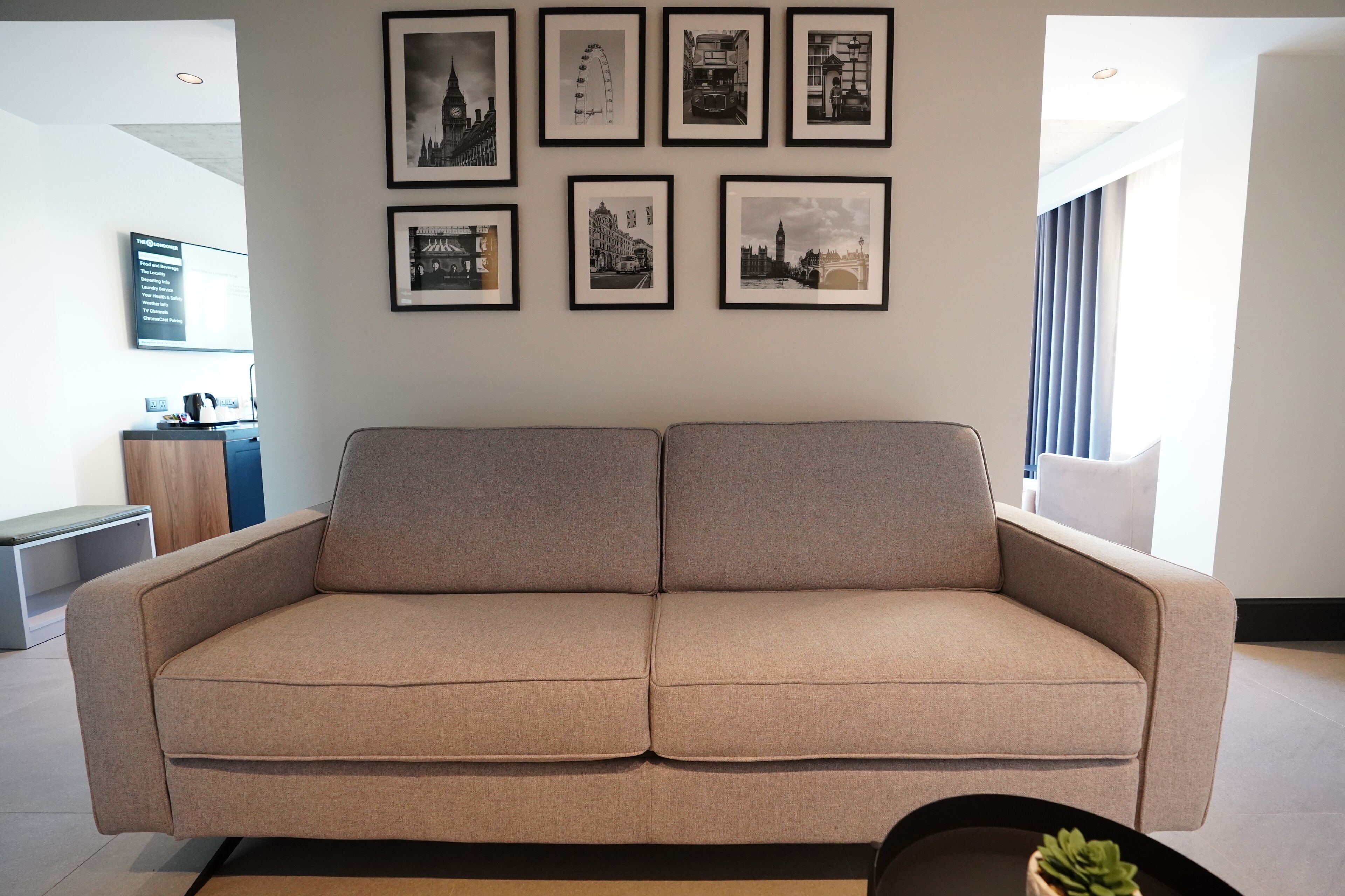 Uma sala de estar moderna com um sofá bege, uma mesa de centro e quadros com paisagens urbanas nas paredes.