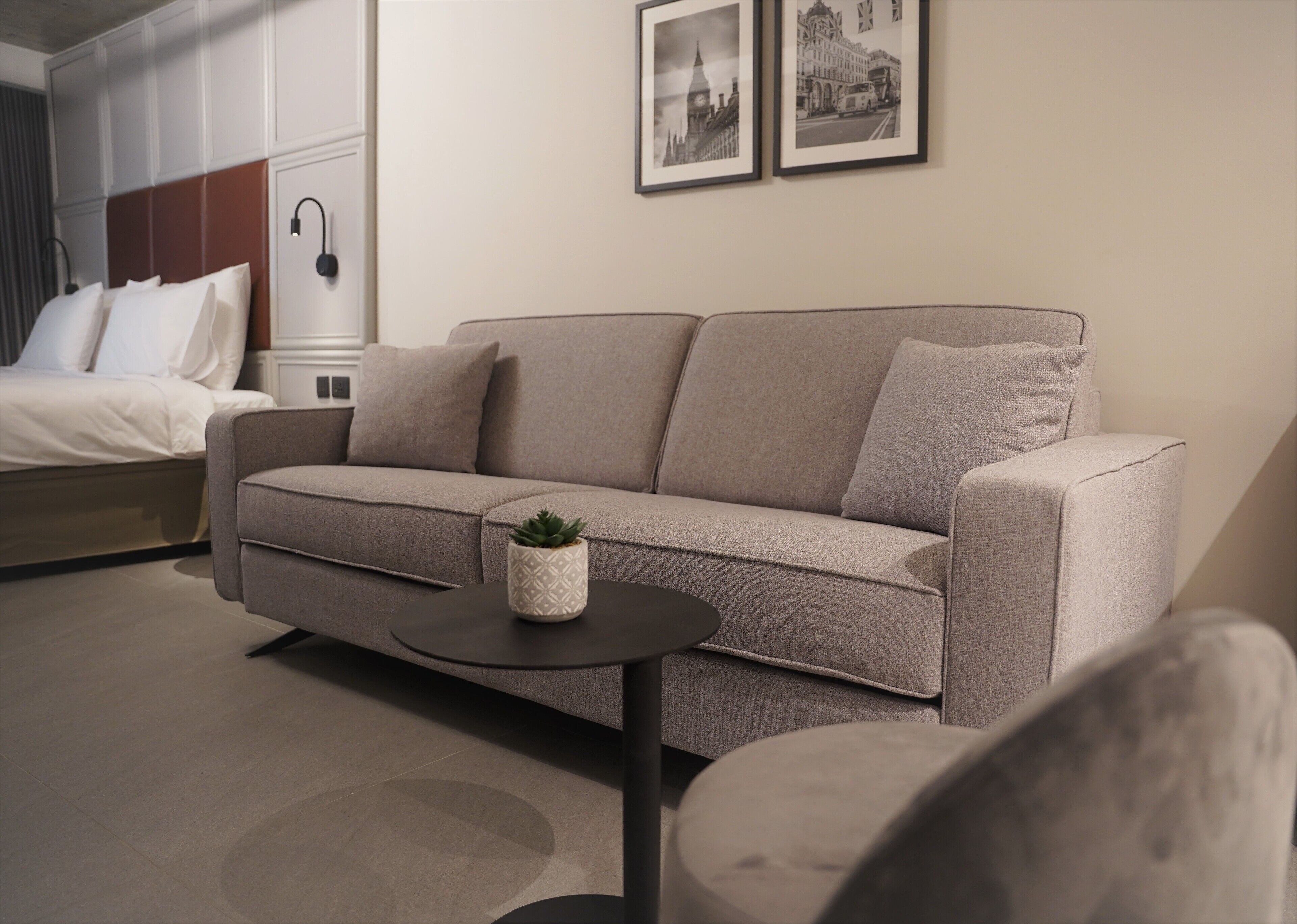 Uma sala de estar moderna com um sofá, uma mesa pequena com uma planta e uma cama ao fundo.