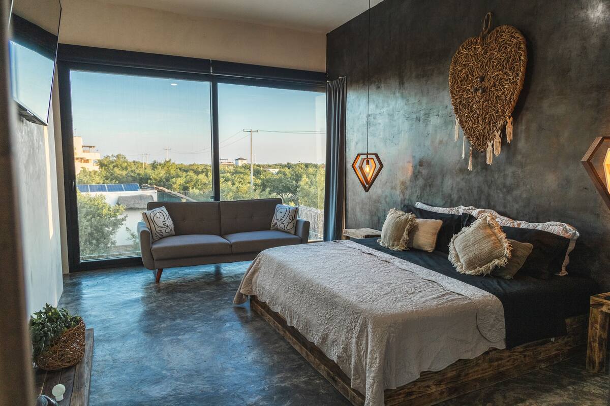 Quarto moderno com uma cama grande, um sofá e vista para o exterior.