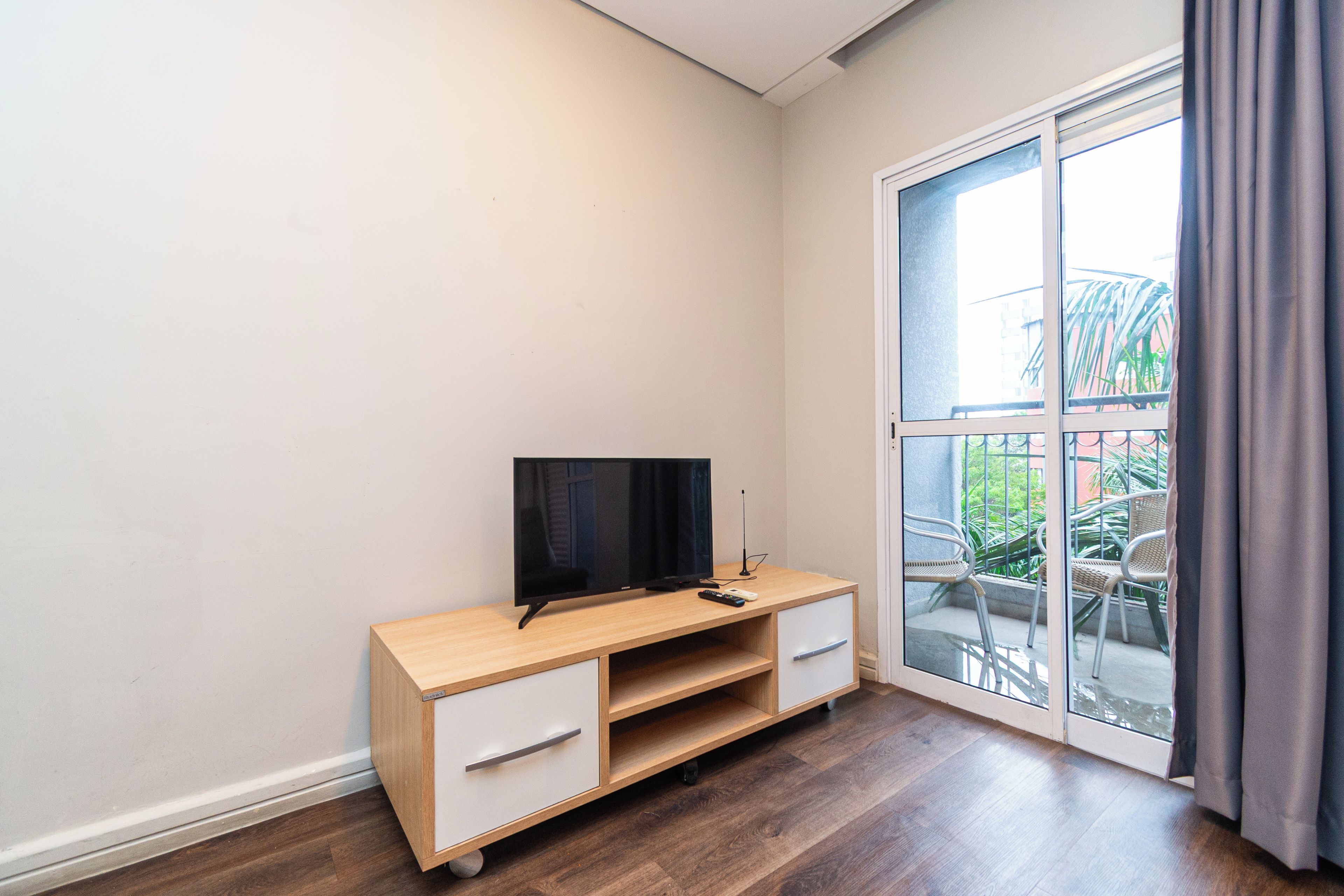 Quarto com estante de madeira para TV, televisão de tela plana e porta de vidro deslizante para uma varanda.