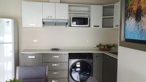 Uma cozinha compacta com micro-ondas integrado, máquina de lavar louça e frigorífico pequeno.