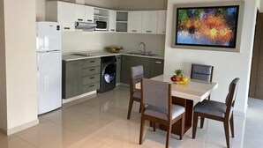 Cozinha moderna com armários brancos, forno embutido e máquina de lavar. Há uma área de jantar com mesa e cadeiras.