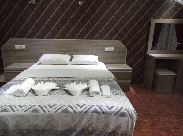 Cama bem arrumada com colcha estampada, dois travesseiros e toalhas dobradas no painel da cabeceira.