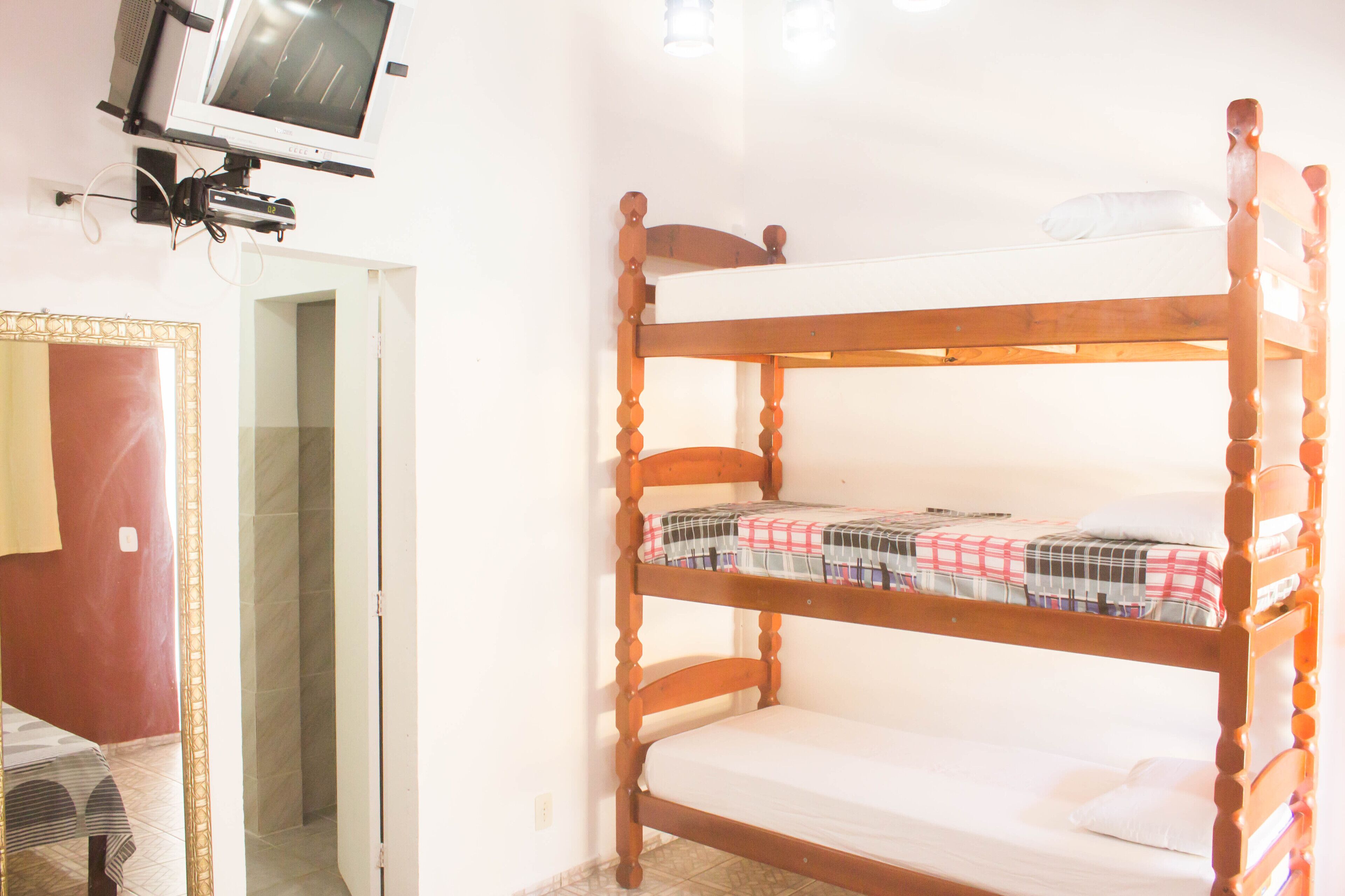 Uma cama beliche com uma televisão montada acima, uma porta para outro quarto e um espelho à esquerda.