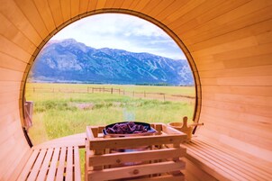 Uma sauna de madeira com uma janela circular, um banco de madeira e uma pequena mesa com uma toalha.