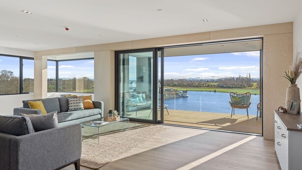 Sala de estar ampla com uma grande porta de vidro deslizante que dá para uma varanda com vista para um lago e montanhas.