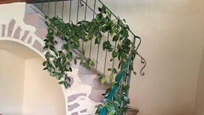 Escadaria com parede de pedra e corrimão de metal coberto por trepadeiras verdes.