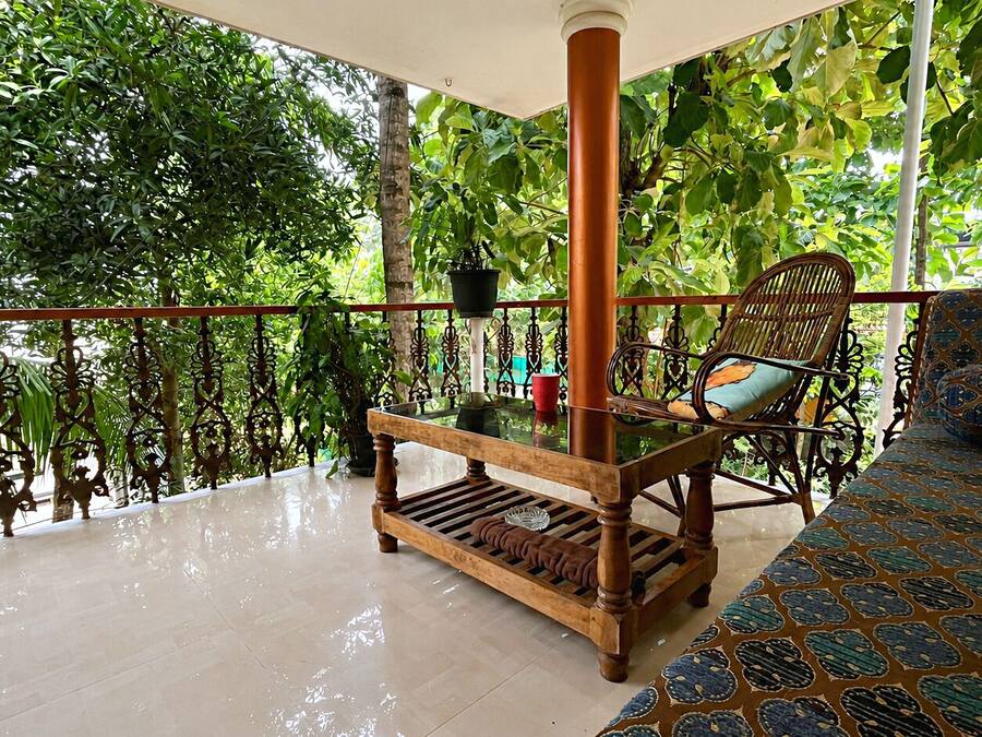 Uma varanda com um banco de madeira, um sofá estampado e um vaso com planta.